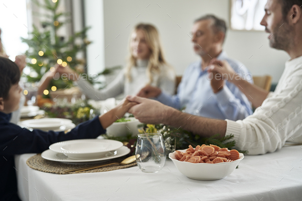Caucasian family sitting around the table, holding hands and praying ...