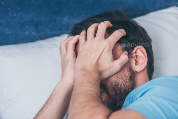 grieving man lying in bed, covering face with hands and crying at home ...