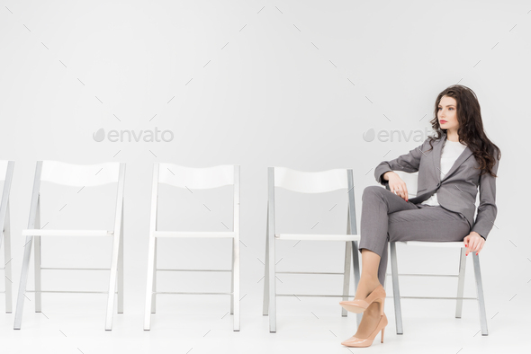 serious woman sitting with crossed legs on chair isolated on grey Stock ...
