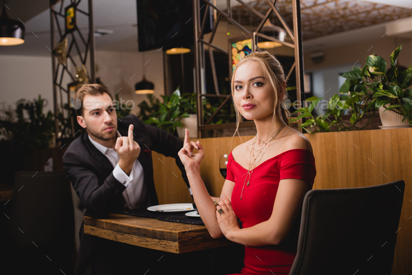 emotional couple showing middle fingers to each other in restaurant ...