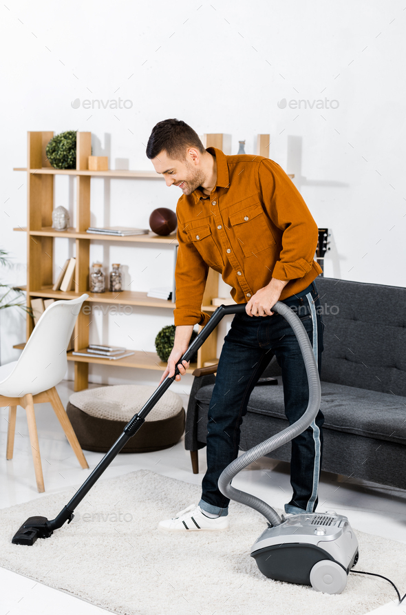 handsome man in modern living room smiling and cleaning house with ...