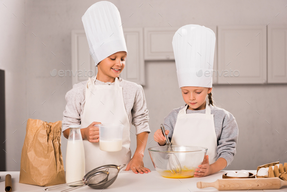 brother and sister in chef hats and aprons whisking eggs in bowl at ...
