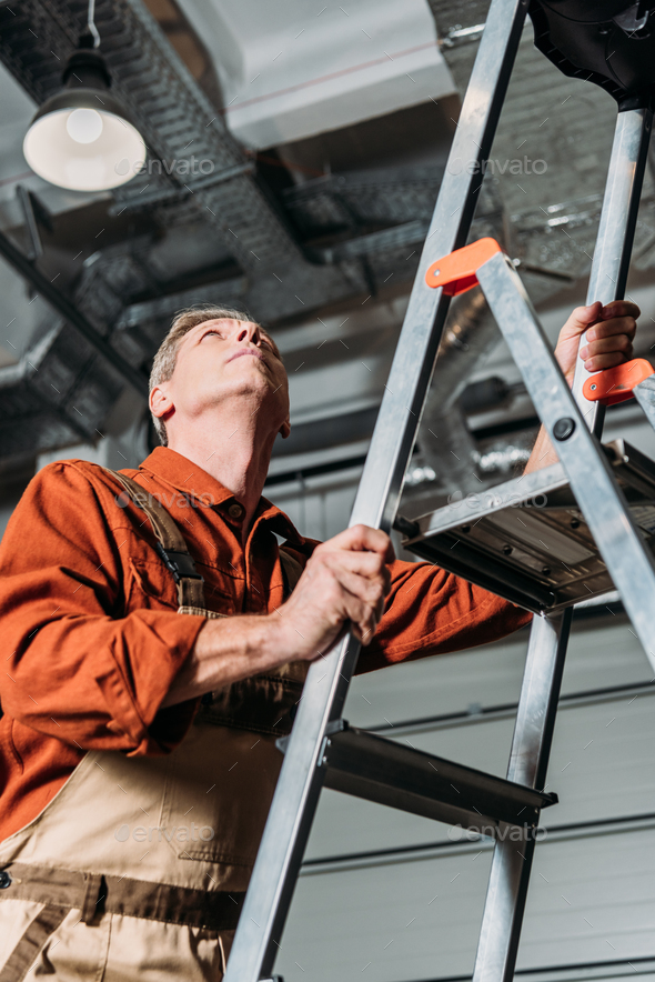 repairman in orange uniform standing on ladder in garage Stock Photo by ...