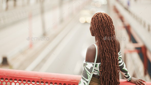 Gorgeous woman with African braids wearing top stands on the bridge ...