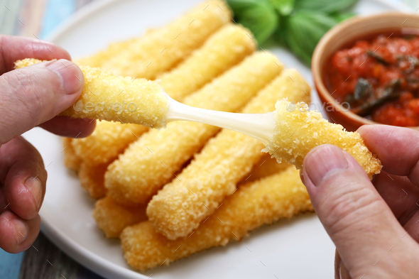 Breaking freshly fried mozzarella sticks and stretching cheese with ...