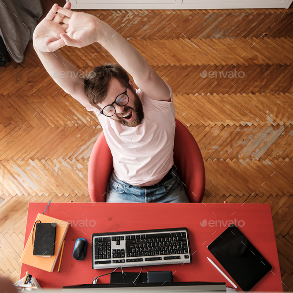 Man is resting, yawns and stretches, working remotely on his computer ...