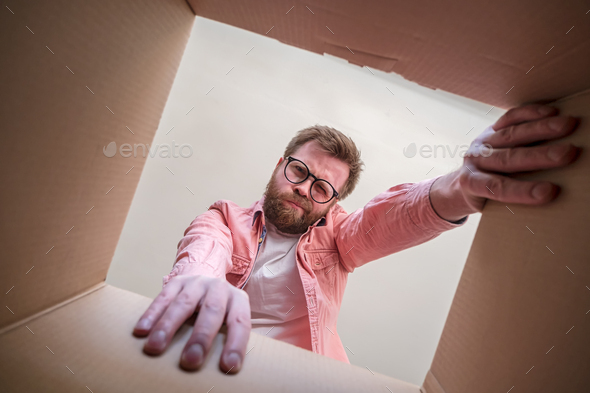 Man with glasses looks into unpacked delivered box with package with ...