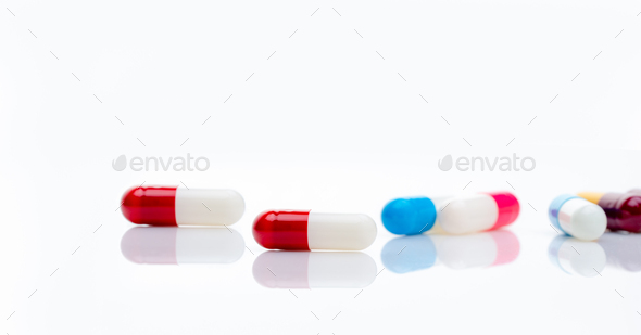 Red-white antibiotic capsule pill on blur multi-colored capsules ...
