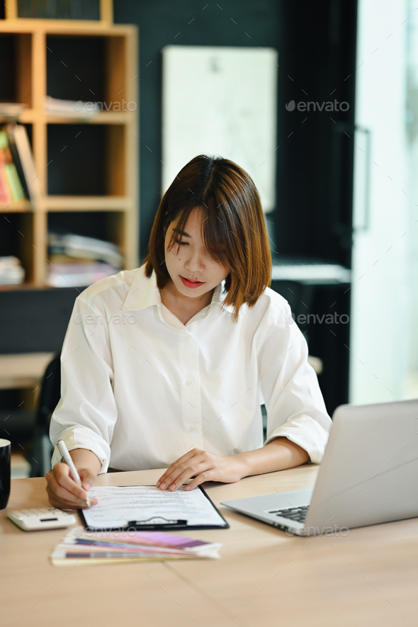 Focused asian woman employee working with laptop and checking financial ...