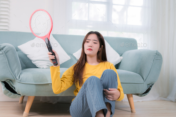Young asian woman using mosquito swatter, electric net racket in living ...