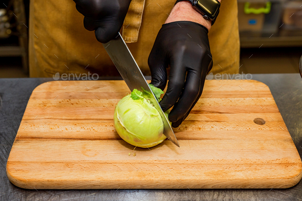 Chef in the kitchen cutting turnip on a wooden board with a big knife ...