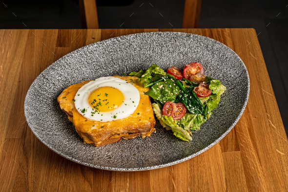Croque madame breakfast served on a grey plate with salad mix and ...
