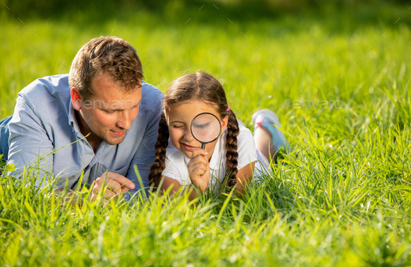 Father and daughter watching bugs in the grass using magnifying glass ...