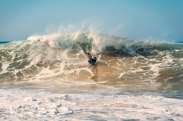 surfer slides with his bodyboard by a huge wave Stock Photo by Raul_Mellado