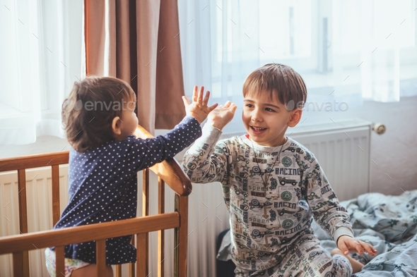 Little sister and brother smiling and playing in kids room . Baby hi five her brother Stock ...