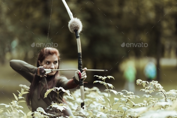Archer woman shooting the bow and arrow in the swamp. Stock Photo by ...