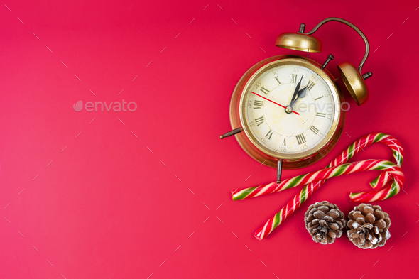 Bronze alarm clock, candy cane and fir cones on red background ...