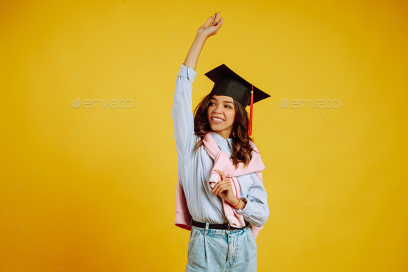 Graduate woman in graduation hat on her head posing on yellow ...