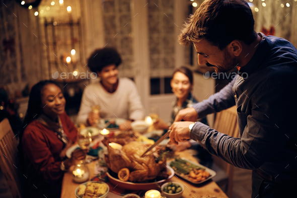 Smiling man carving Thanksgiving turkey during dinner in dining room ...