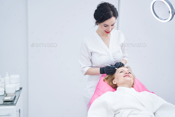 Cheerful beautician drawing marks on woman face in beauty salon Stock ...