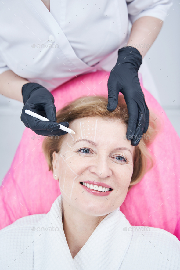 Beautician drawing marks on woman forehead in beauty salon Stock Photo ...