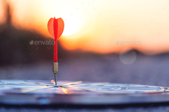 Close up red dart arrow hitting target center dartboard on sunset ...