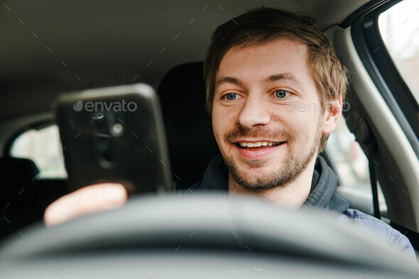 Young smiling male driver using smartphone behind the wheel of the car ...