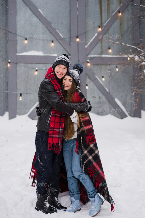 Cheerful loving couple in warm cozy clothes hugging and warming up with ...