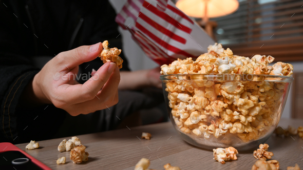 Close up view man hand grabbing popcorn from a glass bowl and watching ...