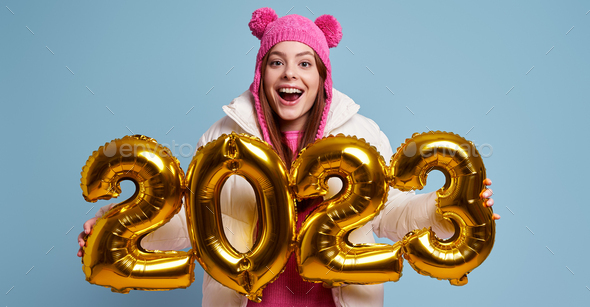 Excited young woman in winter coat holding gold colored numbers against ...