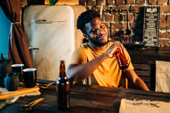 Young attractive black man drinking beer bottle in the dark room or bar ...