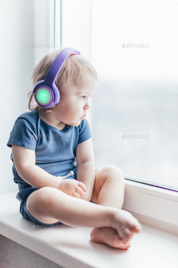 the kid sits by the window and listens to music in headphones very peri ...