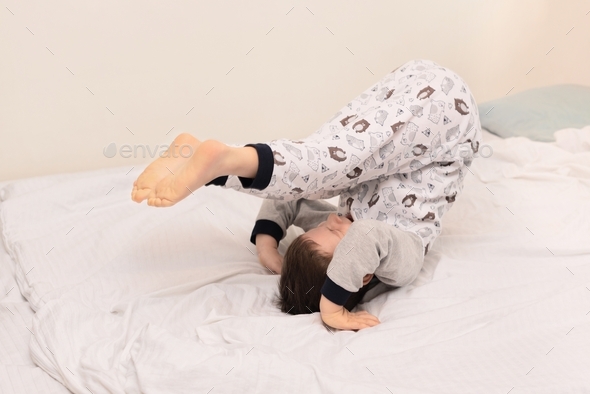 Child boy tumbling on the bed at the morning. Relaxing at home concept ...