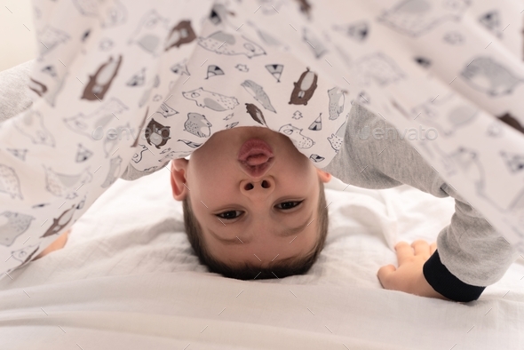 Child boy standing upside down and showing tongue on his bed at the ...