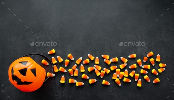 Candy corn candies spilled out of pumpkin basket. Traditional sweets ...