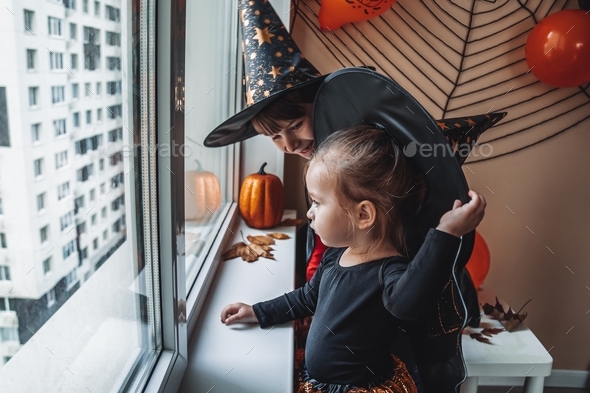 Children in Halloween costumes and witch hats look out the window ...