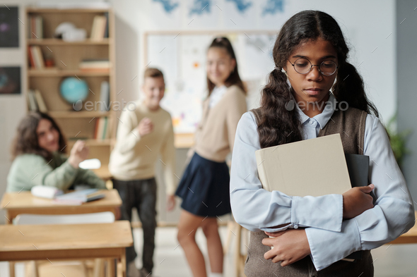 Pre-teen upset schoolgirl standing against three classmates bullying ...