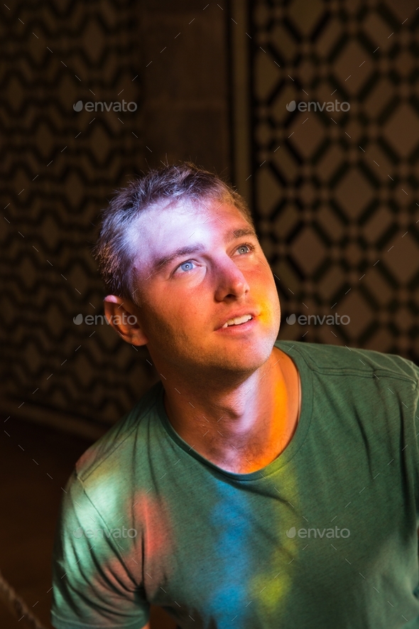 A man looks through a stained glass window while colorful light ...