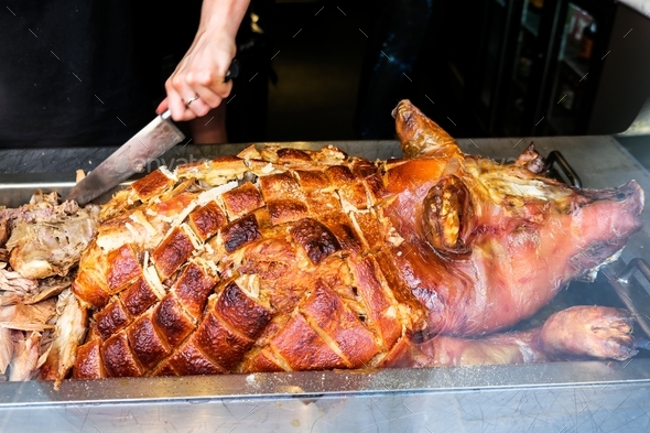 Hand cutting meat from roasted hog on a spit Stock Photo by iportret