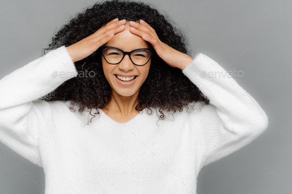 Indoor shot of glad optimistic dark skinned lady touches forehead, has ...