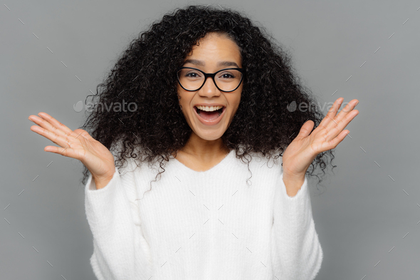 Optimistic lovely young female spreads hands, laughs happily at sees ...