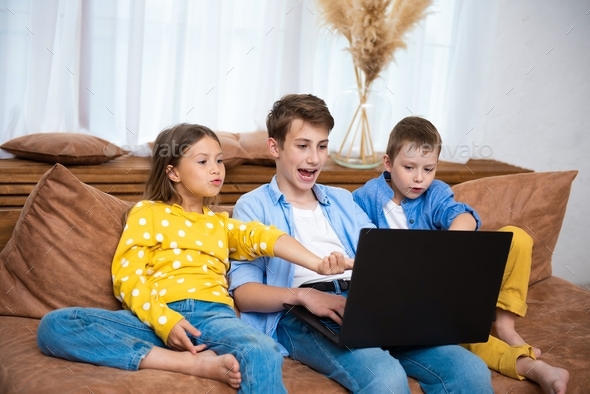 Happy children kids having fun using laptop together sitting on sofa ...