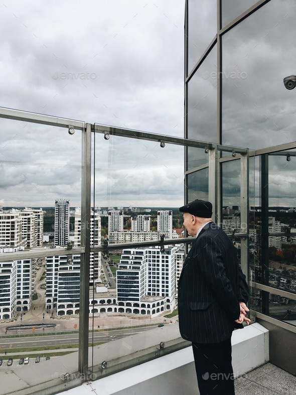 People in the city. Old man standing on building top and watching at ...