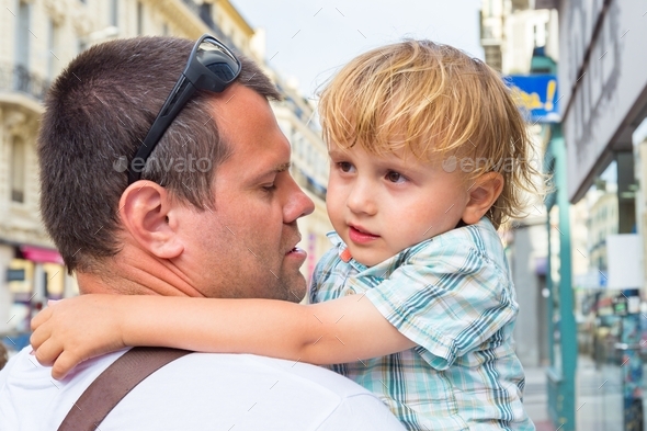 Father holds a tired child in his arms while walking around the city ...