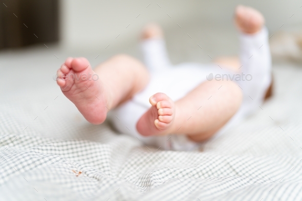 Baby tiny legs close up. Newborn wearing body lying on bed, first days ...