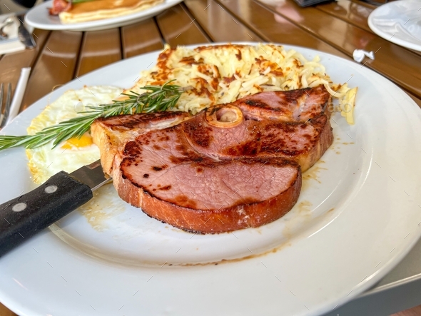 Grilled center cut ham steak, two eggs, hash browns breakfast on white ...