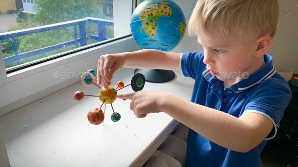 The child points his finger at the model of the solar system, which he ...