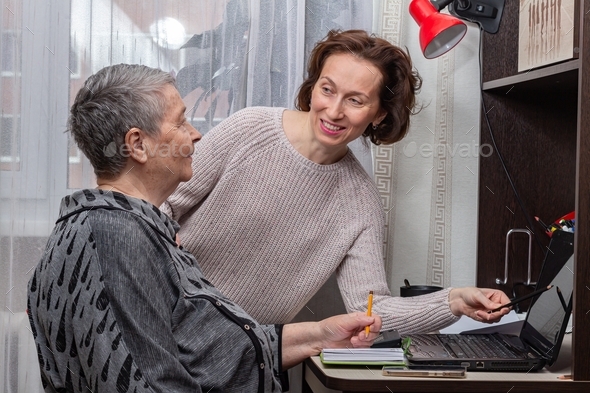 daughter shows her mother how to use computer, laptop, teaches how to ...