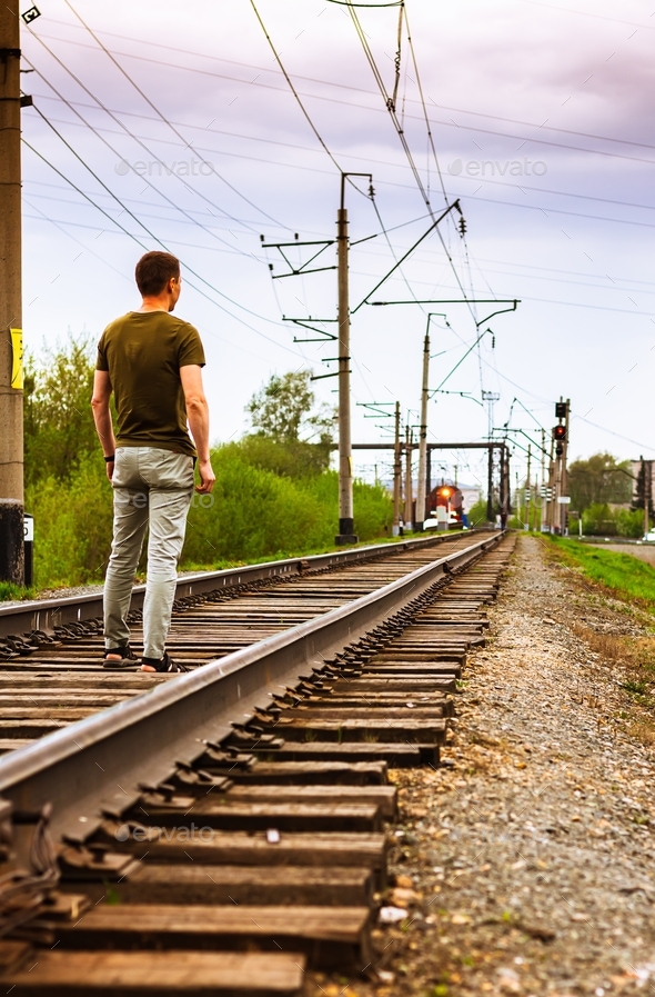 man stands on railroad tracks, train rides on tracks.red traffic light ...