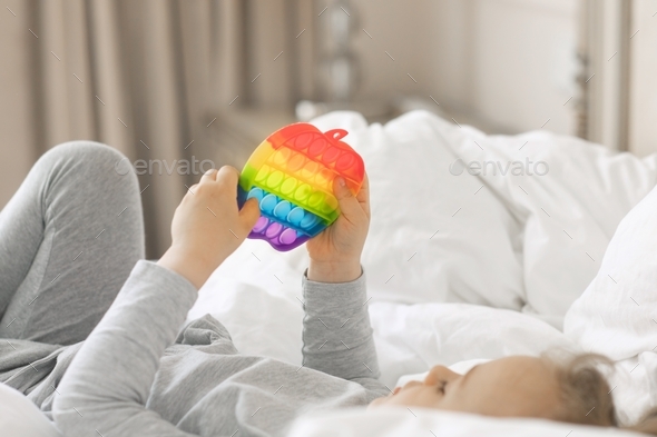 Child playing and relaxing with pastel Pop It toy fidget lying on white ...
